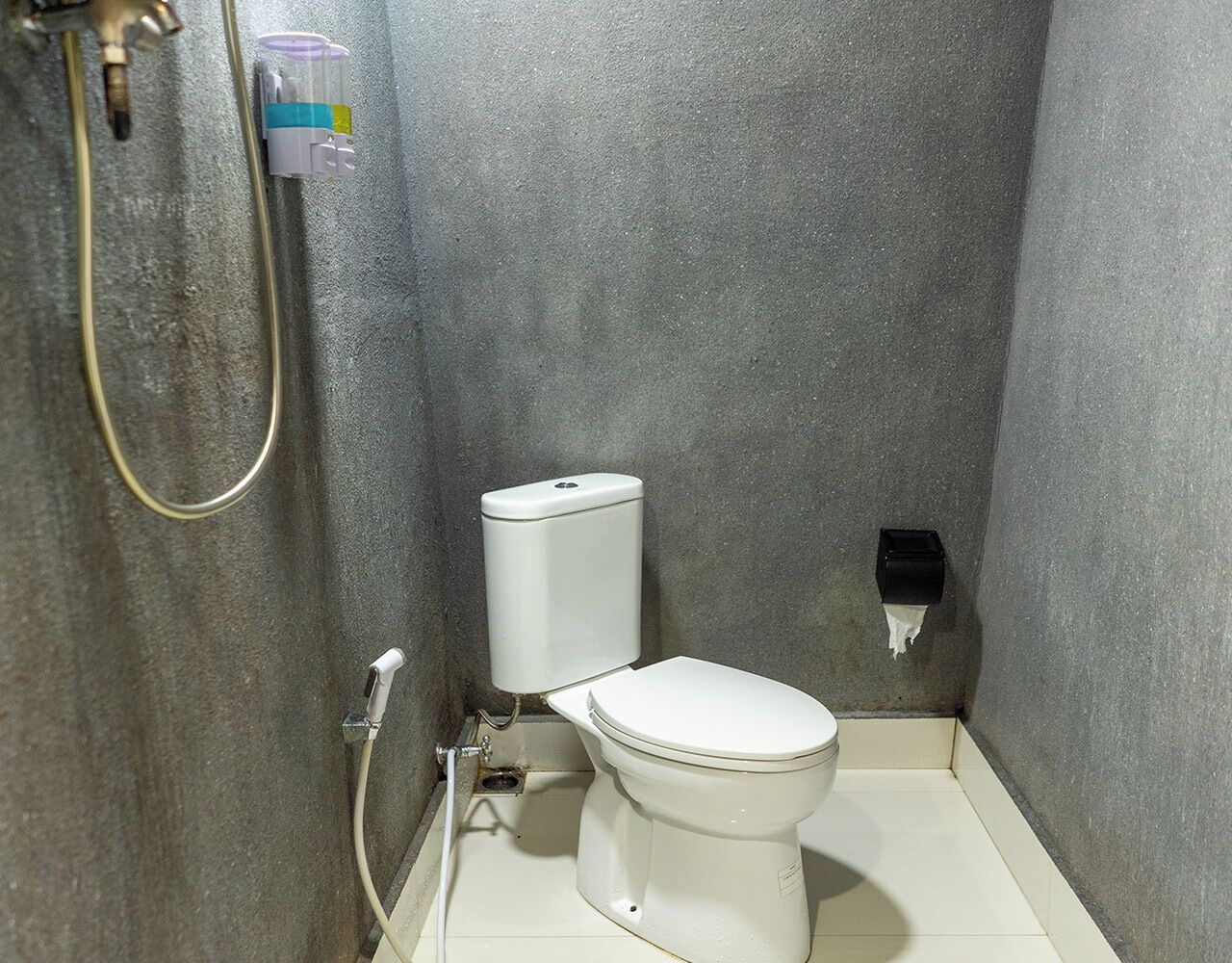 Casa de banho pequena e compacta, com sanita branca, chuveiro e secador de mãos.