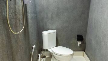 Casa de banho pequena e compacta, com sanita branca, chuveiro e secador de mãos.