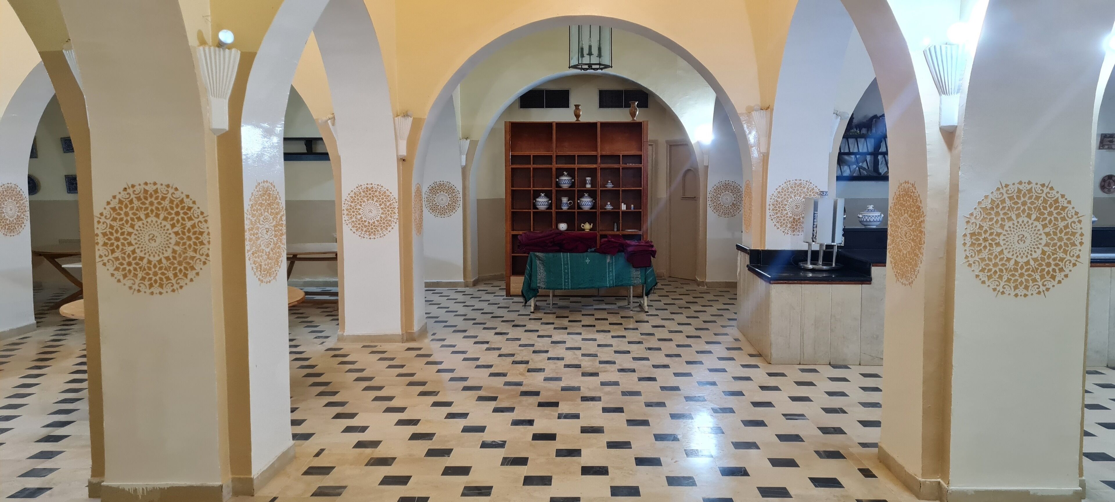 Quarto com piso xadrez, portas em arco e uma área de estar central com tecido verde.