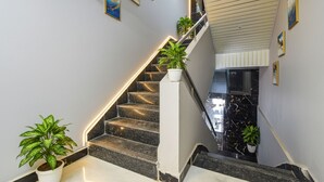 Escadaria moderna com degraus de mármore preto, paredes brancas e corrimão de madeira. Vasos com plantas na base e no patamar.