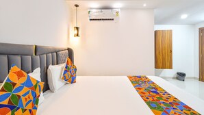 Quarto de hotel moderno com cama grande, cabeceira, ar condicionado fixado na parede, luminária de cabeceira e guarda-roupa de madeira.