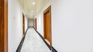 Um corredor comprido e estreito com portas de madeira em ambos os lados e piso de mármore.