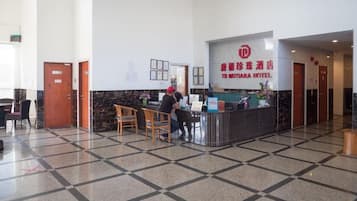 Uma área de recepção de hotel com balcão de check-in, cadeiras e piso ladrilhado.