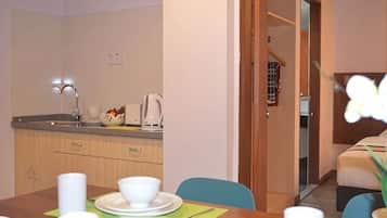 Espaço de refeições com mesa posta para dois, área de cozinha com pia e armários, e escada que dá acesso a outro quarto.