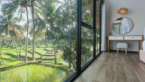 Quarto com uma grande janela que oferece vista para uma paisagem verde exuberante, com palmeiras e campos em terraços.