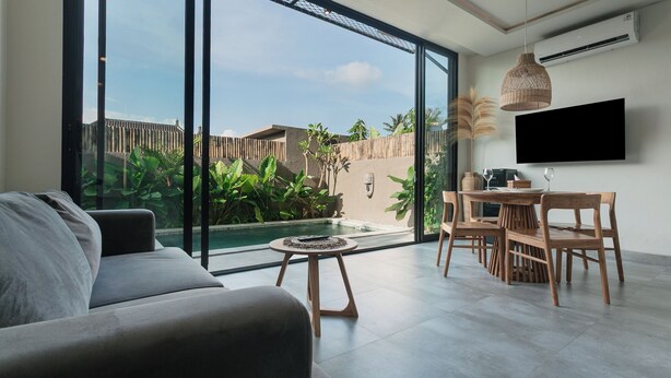 Uma sala de estar moderna com uma grande porta de vidro que dá para uma área de piscina, uma televisão de tela plana na parede e um conjunto de jantar.