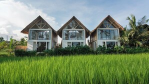 Uma villa moderna com design simétrico, apresentando um espaço aberto central e duas alas, rodeada por vegetação exuberante e um campo de arroz.