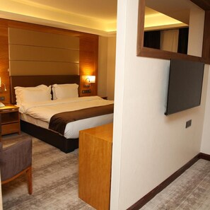 Quarto de hotel com cama, mesa de cabeceira, cadeira e TV de tela plana na parede.