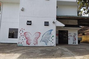 Fachada de prédio com um mural de asas e estrelas, uma porta com uma placa e uma figura pequena.