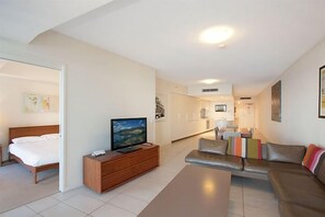 Quarto de hotel moderno com cama, televisão, sofá e área de refeições.