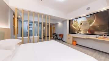 Quarto de hotel moderno com uma cama grande, televisão na parede e um pequeno espaço de estar com mesa e cadeiras.
