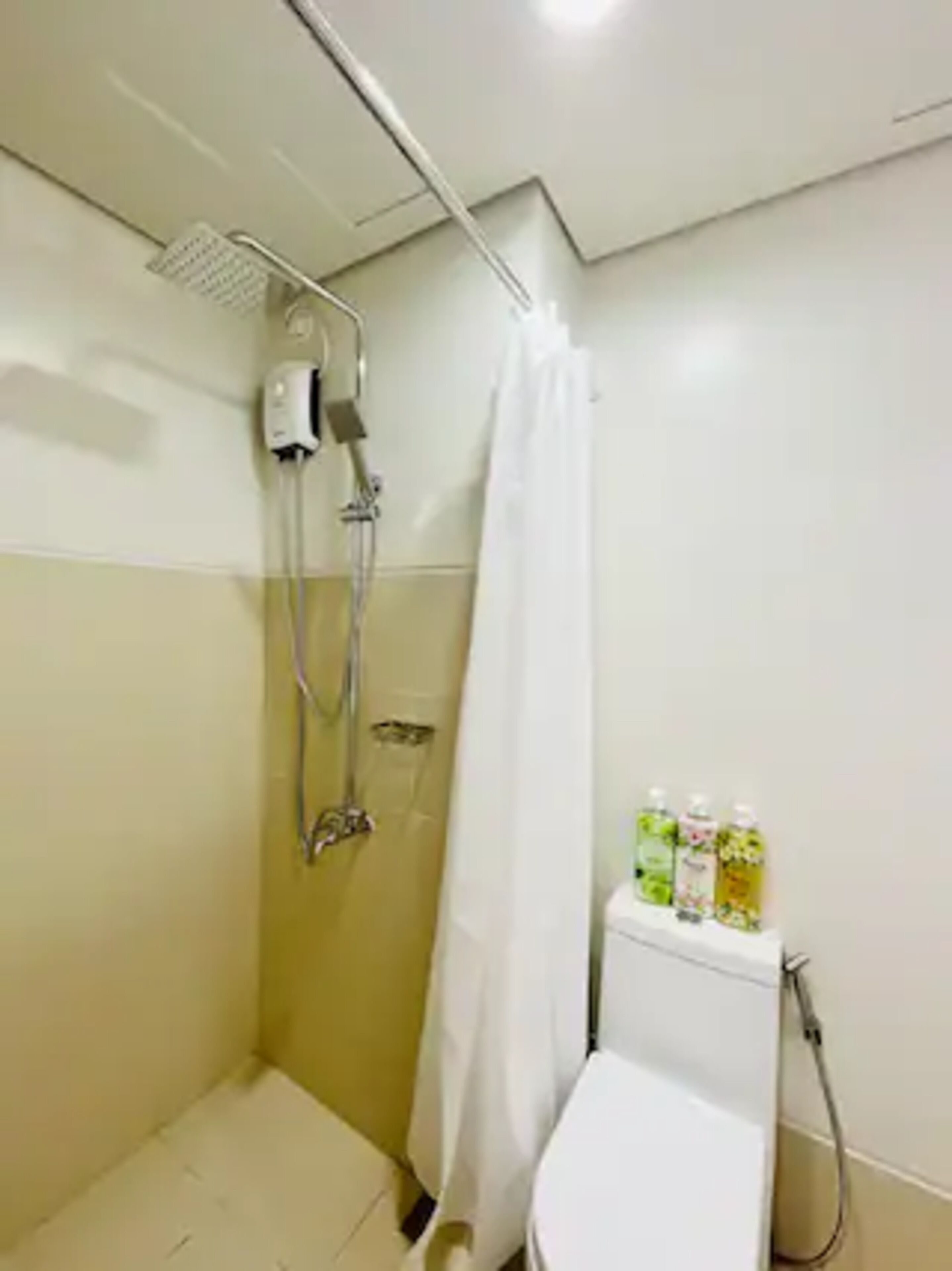 Um espaço de banho pequeno e fechado, com um vaso sanitário e um chuveiro fixado na parede.