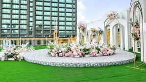 Um hotel com um edifício moderno, uma área externa circular com decorações florais e uma estrutura branca com arcos.