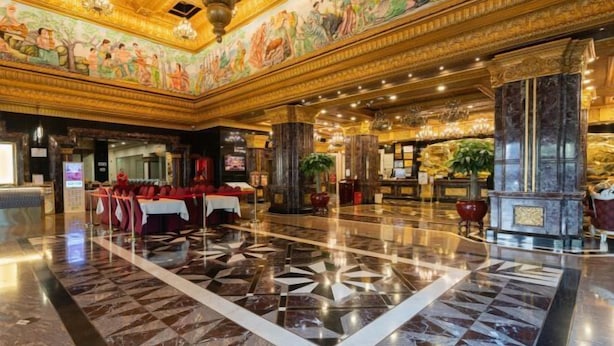 Um amplo hall de entrada com piso de mármore, colunas elaboradas e um grande mural no teto.