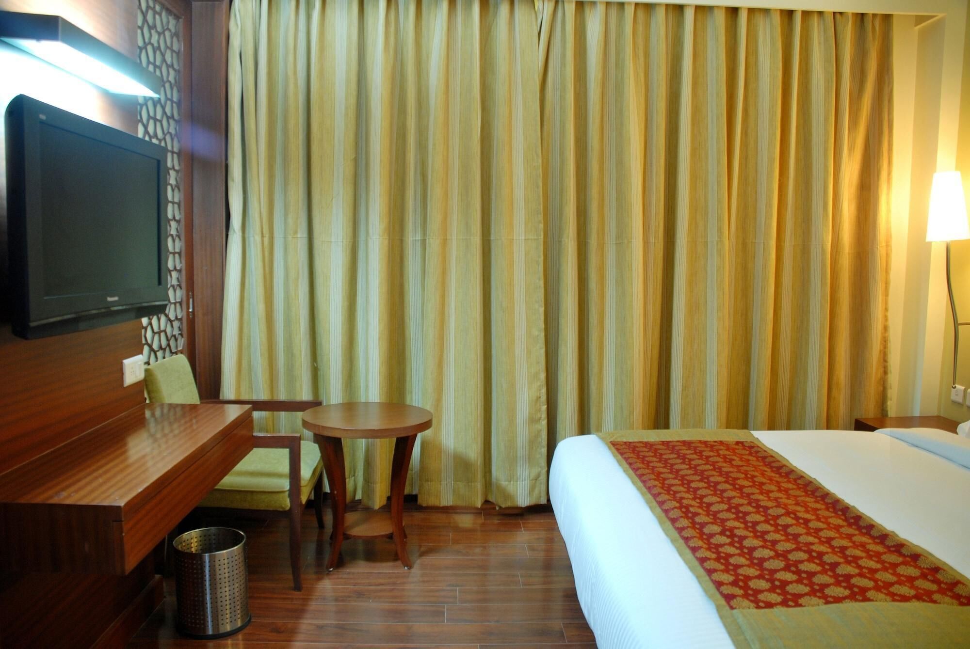 Quarto de hotel com cama, escrivaninha, cadeira, televisão e cortina.