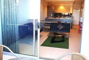 Uma sala de estar moderna com um sofá, um separador de vidro e uma cozinha ao fundo.