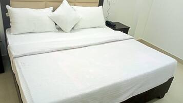 Cama com cabeceira bege, roupa de cama branca e telefone de mesa.