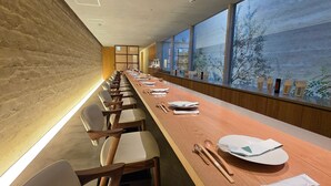 Sala de conferências com uma mesa comprida, cadeiras e vista para árvores através de amplas janelas.