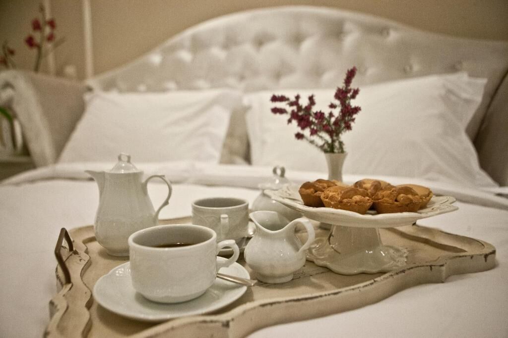 Uma bandeja de café da manhã bem organizada sobre a cama, com um jarro branco, xícaras, jarra e pães.