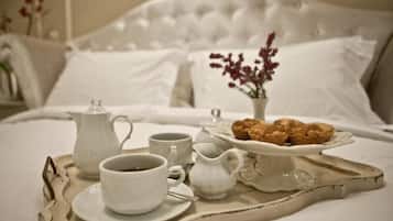 Uma bandeja de café da manhã bem organizada sobre a cama, com um jarro branco, xícaras, jarra e pães.
