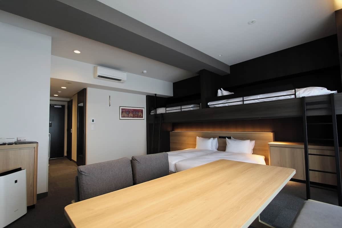 Quarto de hotel moderno com beliches, uma mesa de jantar de madeira e uma cozinha compacta.