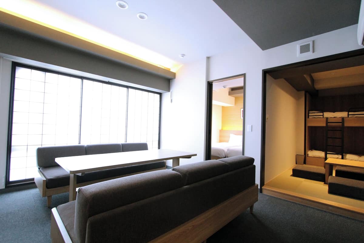 Quarto de hotel moderno com uma janela grande, um sofá, uma mesa e um espaço para a cama embutido.
