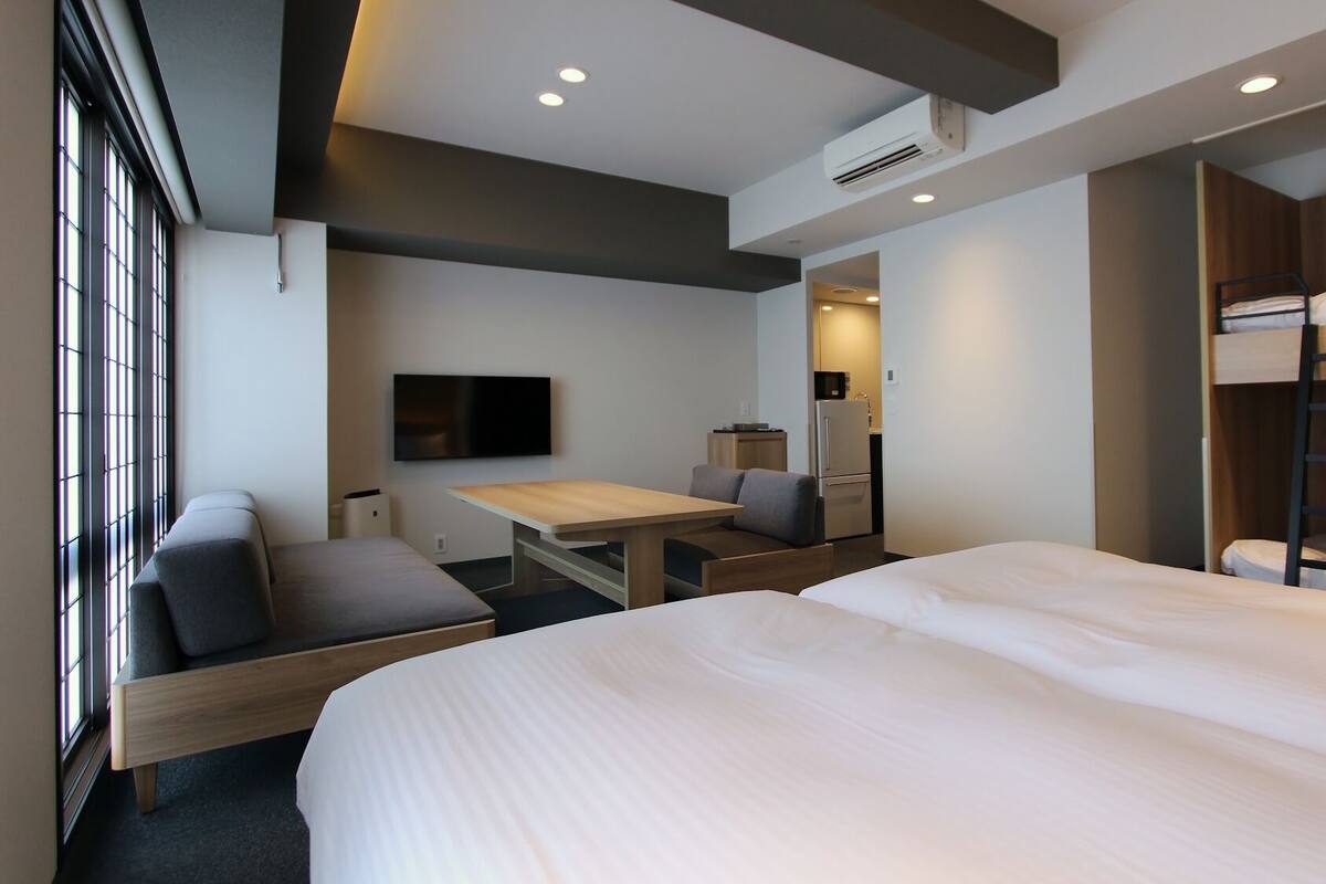 Quarto de hotel com cama, beliches, escrivaninha, cadeira, televisão e ar condicionado.