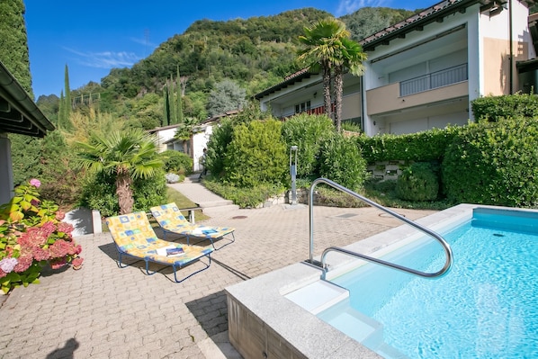 Uma área de piscina com espreguiçadeiras, um deck à beira da piscina e montanhas ao fundo.