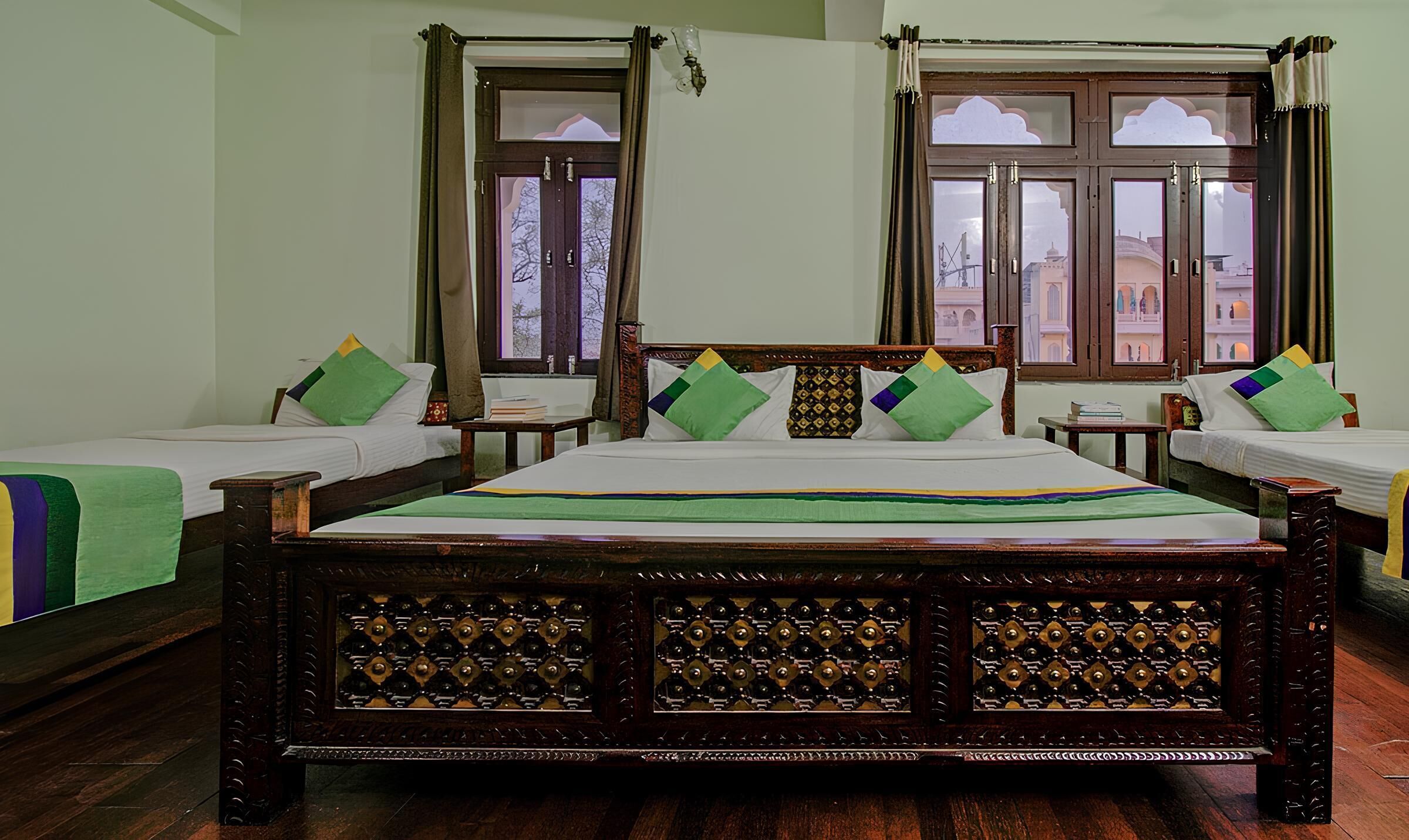 Quarto tradicional com uma cama grande, duas camas menores e uma janela com vista para edifícios.