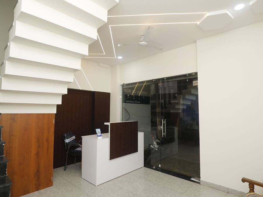 Uma área de recepção moderna com balcão branco, parede de destaque em madeira, porta de vidro para um quarto para não fumantes e escada com acabamento em madeira.