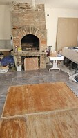 Um quarto com lareira de tijolos, uma mesa de madeira e diversos objetos espalhados.
