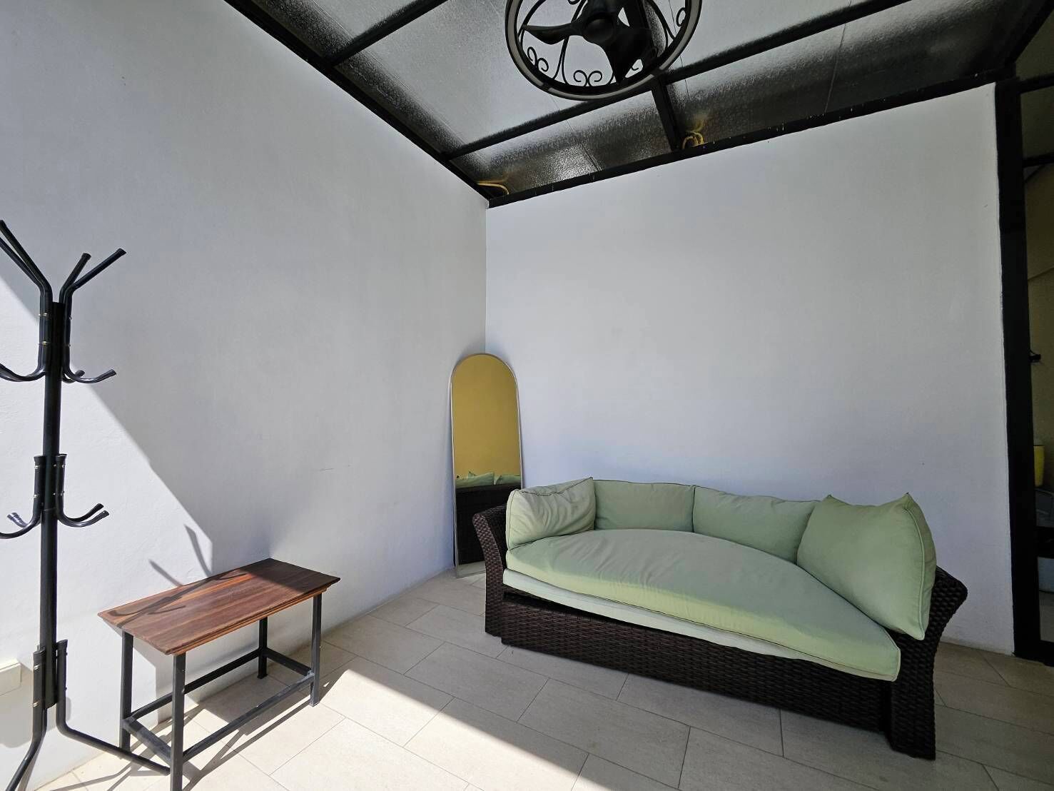 Quarto com sofá estofado verde, uma pequena mesa de madeira, um porta-roupas e um ventilador de teto.