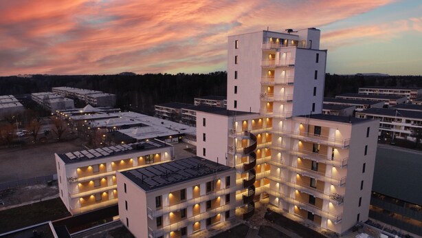 Um hotel com vários andares, uma torre central, diversas varandas e área de estacionamento.
