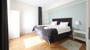 Quarto moderno com uma cama grande, mesa de cabeceira e vista para o horizonte urbano pela janela.