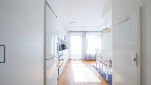 Cozinha clara com geladeira, forno e micro-ondas. Há uma área de refeições com mesa e cadeiras.