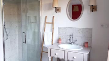 Casa de banho com cabine de duche em vidro, toucador branco com lavatório e duas luzes de parede.