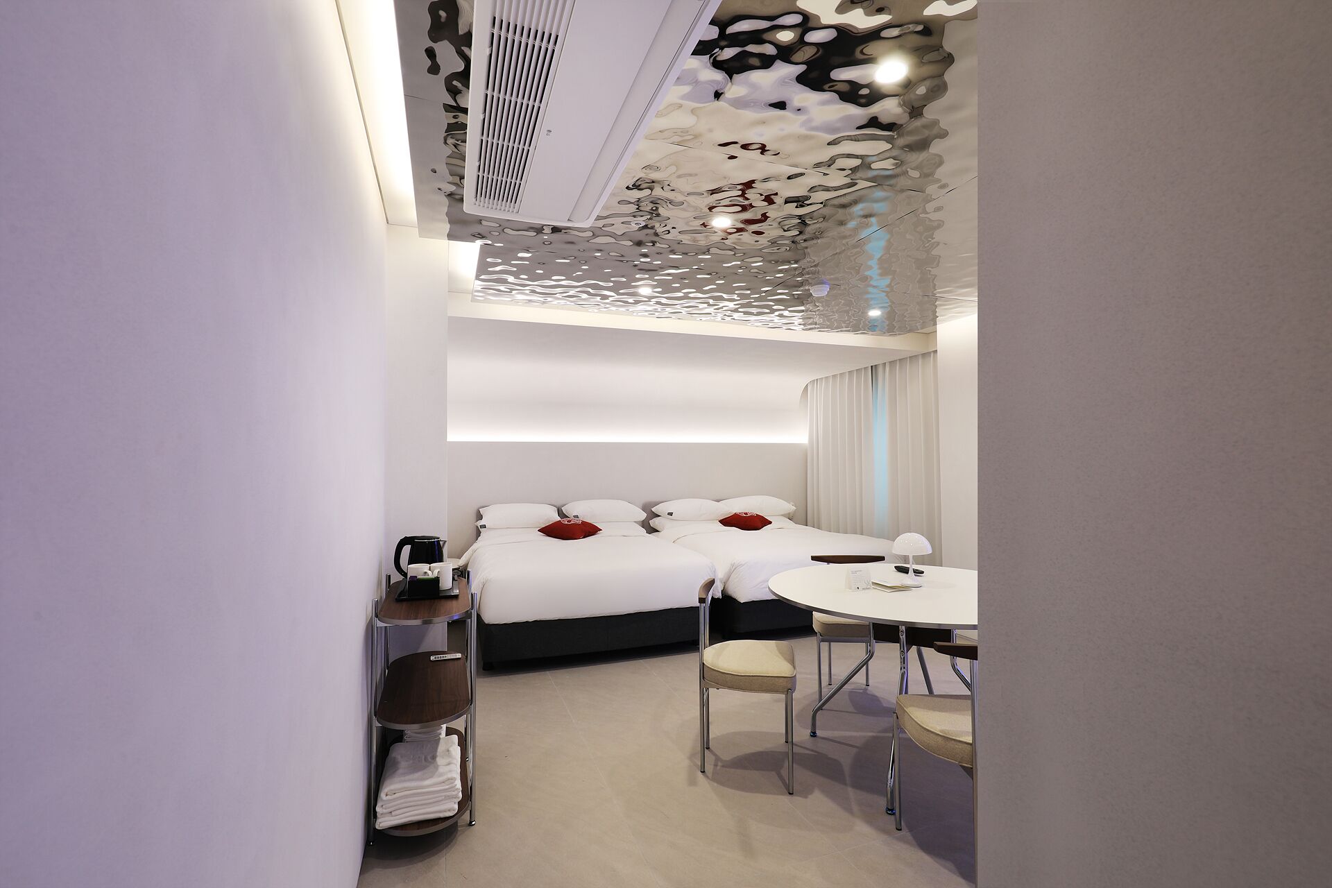 Quarto de hotel moderno com uma cama, duas cadeiras, uma mesinha e teto com design único.