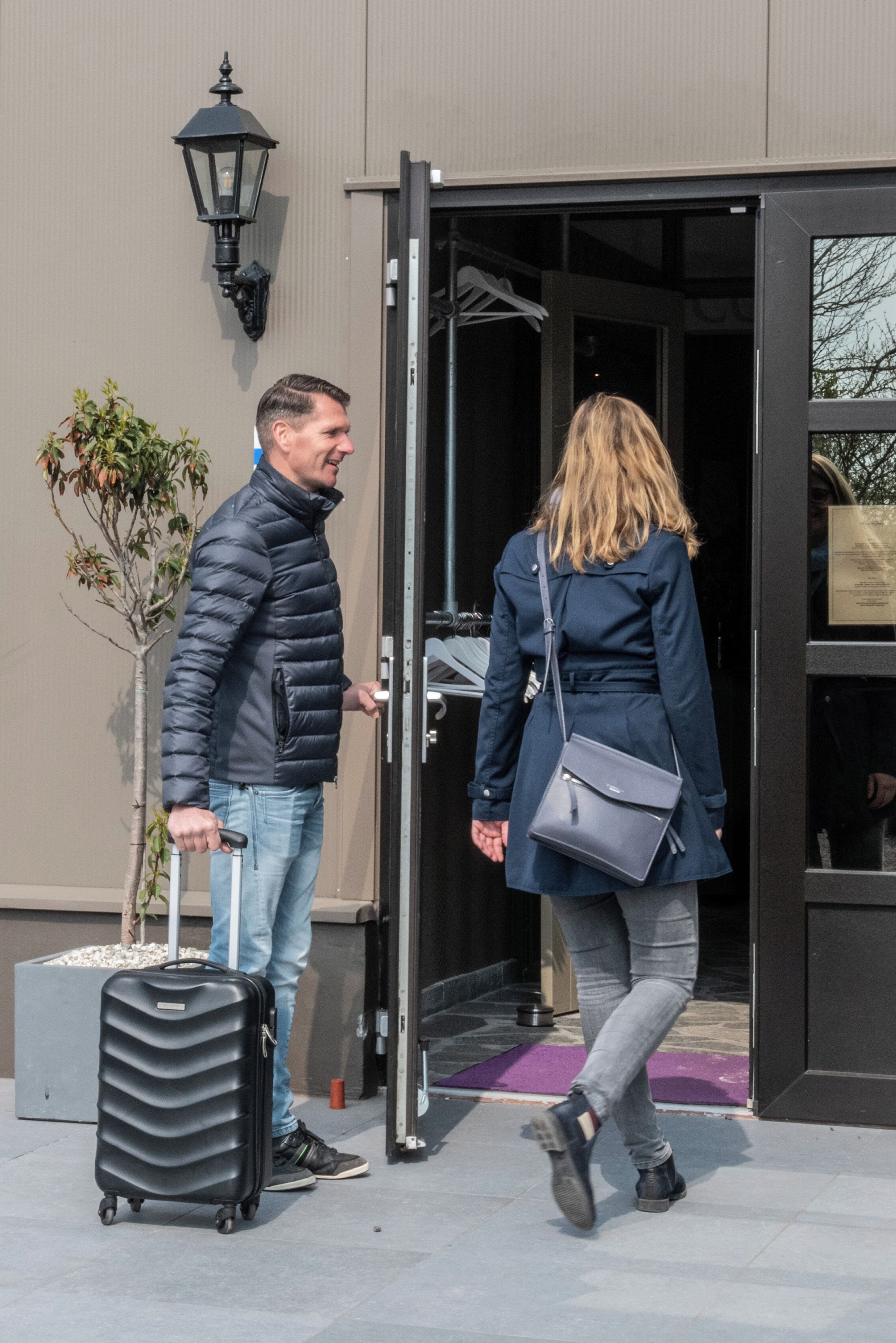Um homem e uma mulher saindo de um edifício carregando uma mala e uma bolsa.