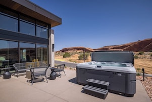 An outdoor patio with a hot tub, wicker furniture, and a view of red rock formations.