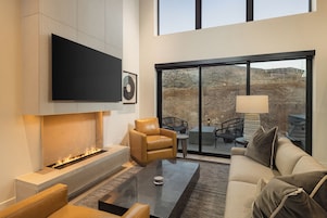 Uma sala de estar moderna com televisão de tela plana, lareira, sofá e uma grande porta de vidro deslizante que dá para uma área externa.