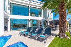 Uma casa moderna de dois andares com piscina, espreguiçadeiras e área de churrasco.