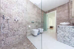 Um banheiro moderno com azulejos estampados, box de vidro, vaso sanitário, bidê e pia.