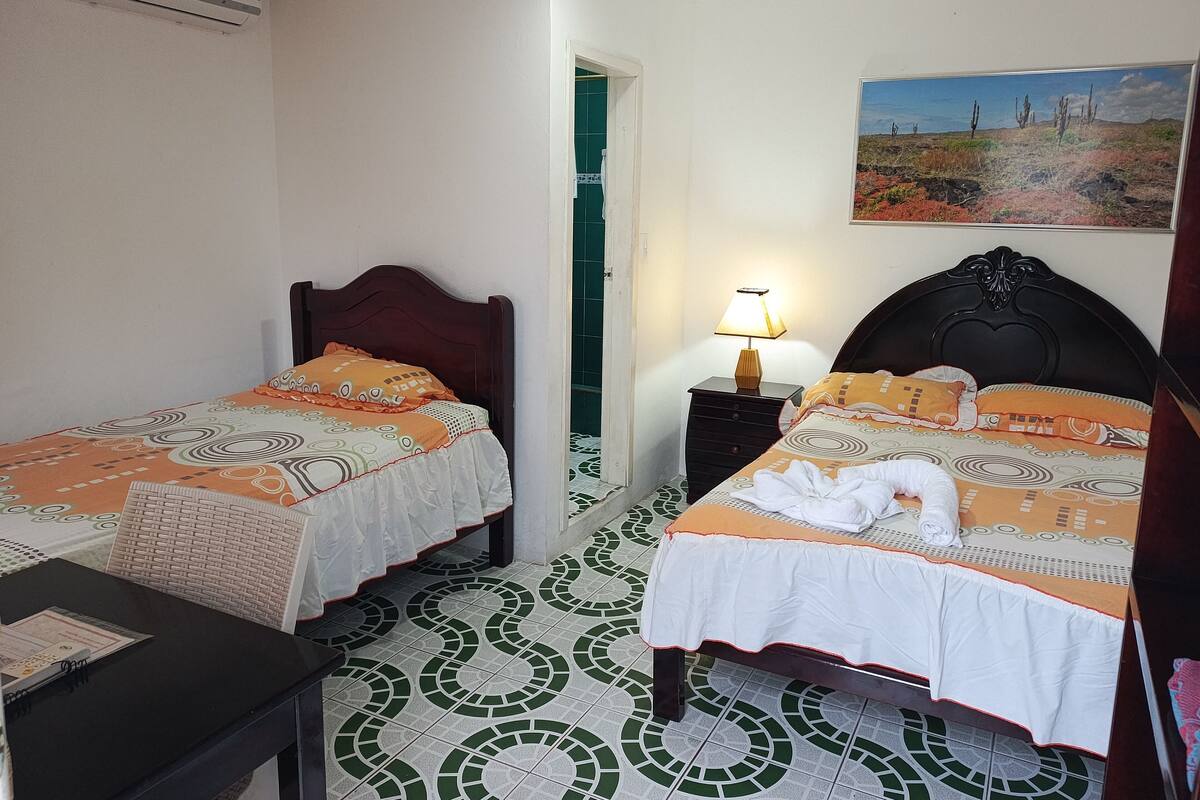 Quarto com duas camas, uma escrivaninha e um quadro na parede.