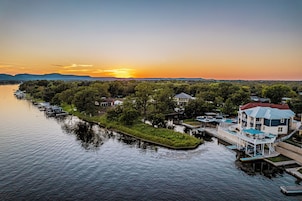 Uma propriedade à beira do lago com barcos atracados, uma casa grande com telhado azul e vegetação ao redor.