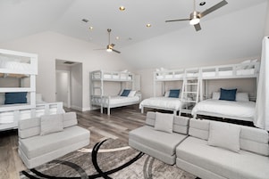 Quarto moderno e bem iluminado com beliches, sofá e ventilador de teto.