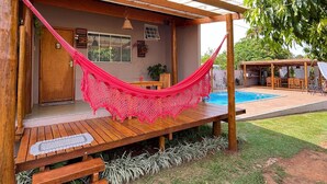 Uma casa de madeira com varanda, rede, piscina e um pequeno jardim.