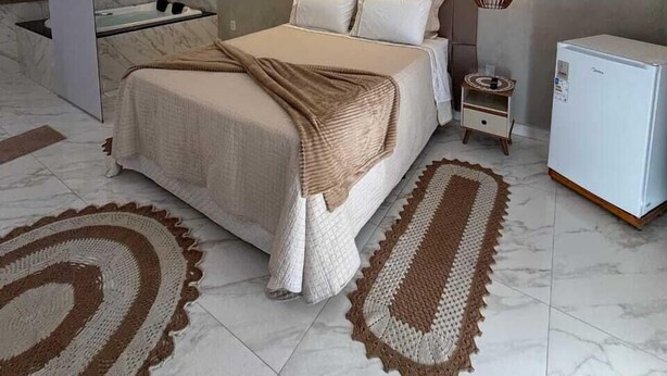 Quarto moderno com uma cama grande, mesas de cabeceira, um pequeno frigorífico e um ventilador de teto.