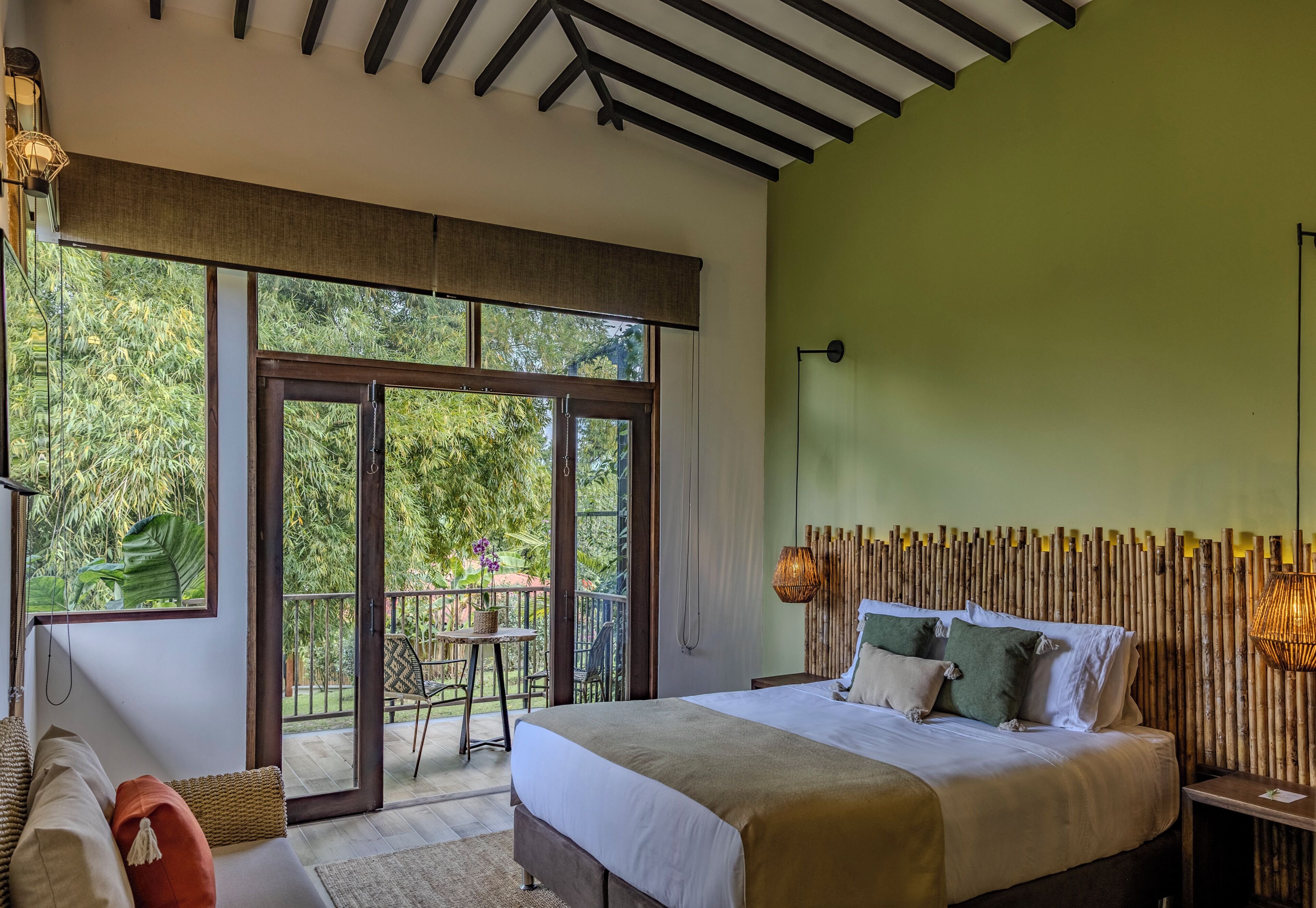 Quarto com cama grande, varanda com mesa e cadeiras e vista para área verde.