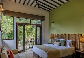Quarto com cama grande, varanda com mesa e cadeiras e vista para área verde.