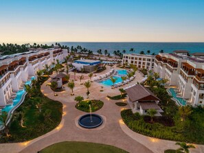 Resort com várias piscinas, uma fonte central e vista para a praia.